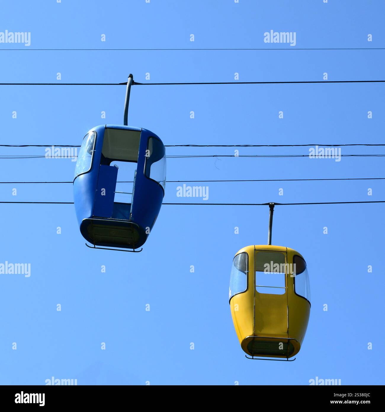 Blue and yellow passenger cable way cabins in the clear blue sky. Blue ...
