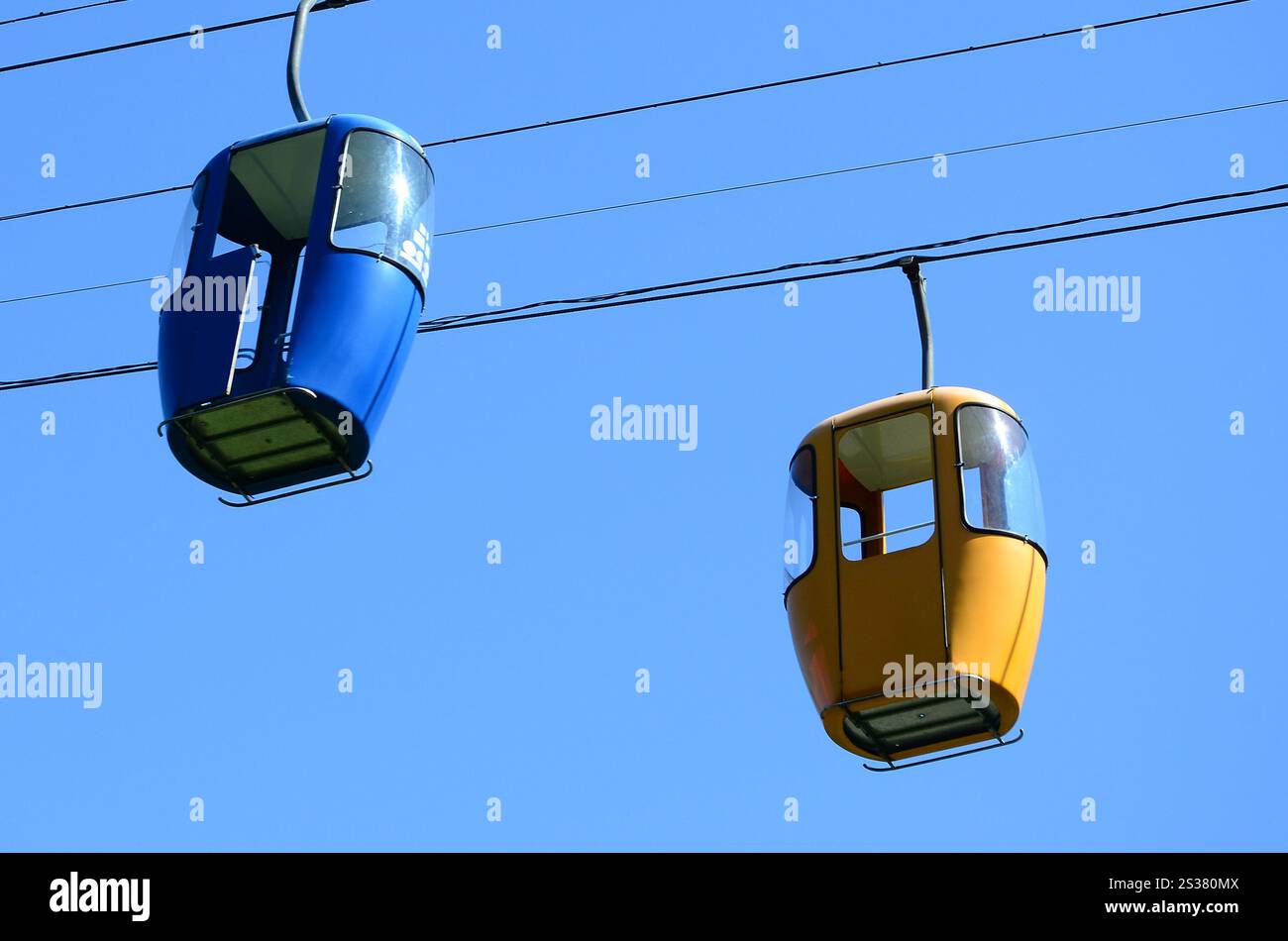 Blue and yellow passenger cable way cabins in the clear blue sky. Blue ...
