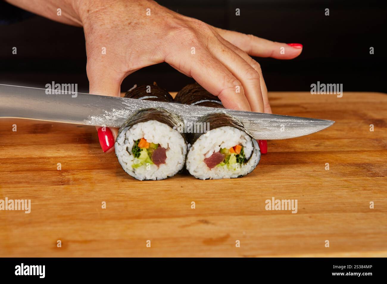 A knife cuts through sushi rolls coated with sesame seeds, presenting a ...