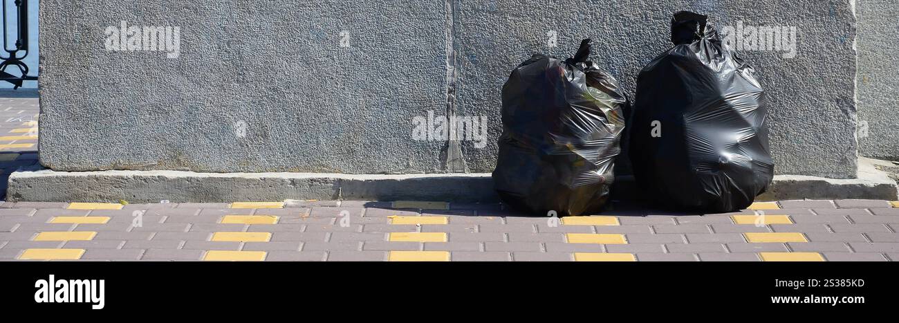Two black garbage bags on tiled street floor at concrete fence in city ...