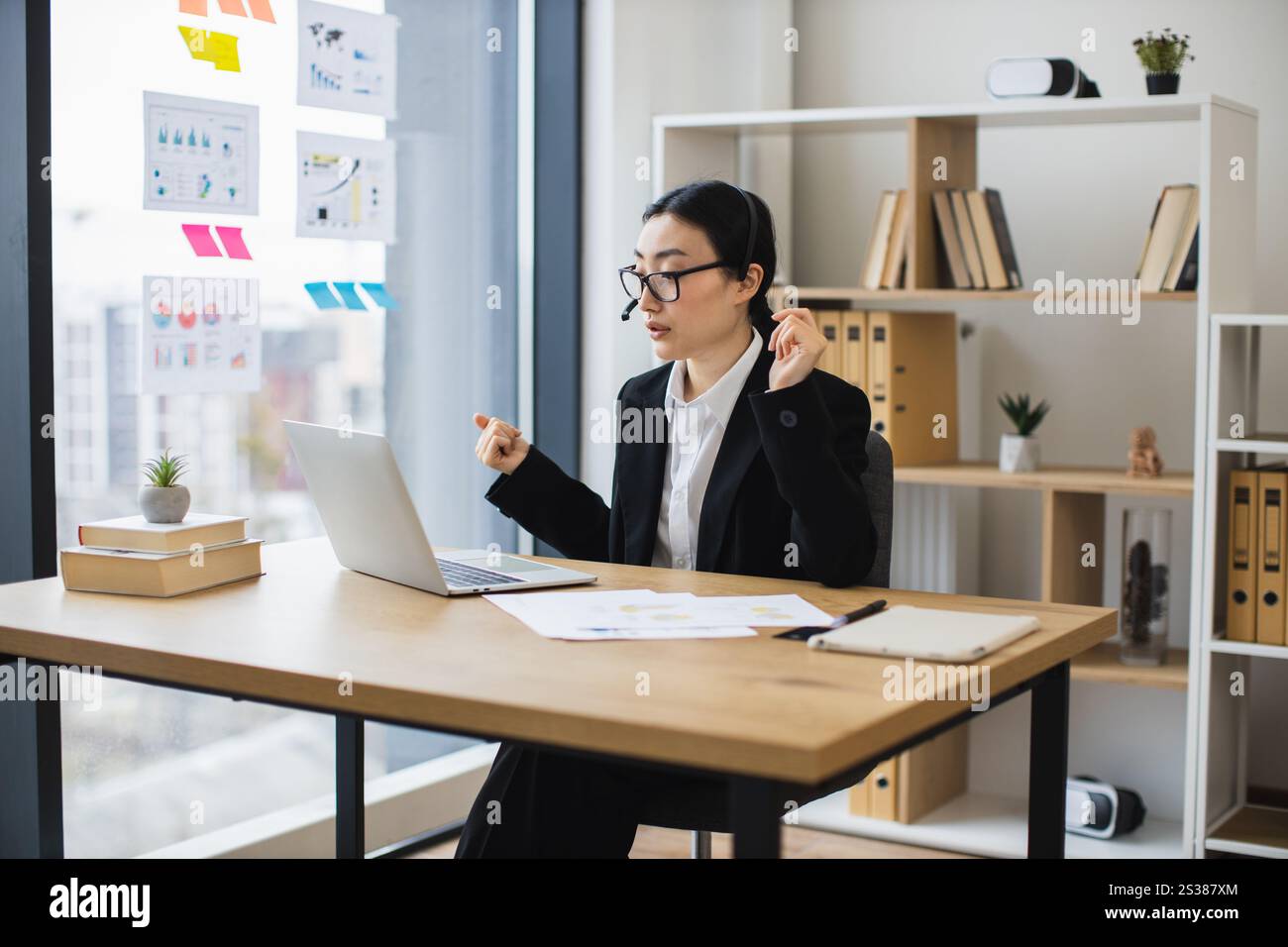 Asian businesswoman wearing headset participating in online meeting ...