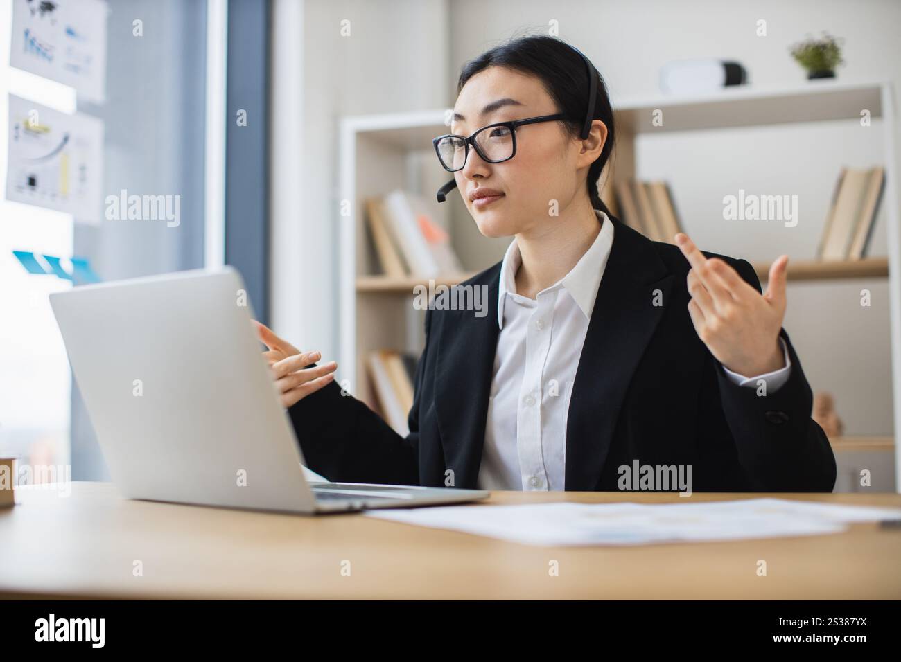 Asian businesswoman wearing headset participating in online meeting ...