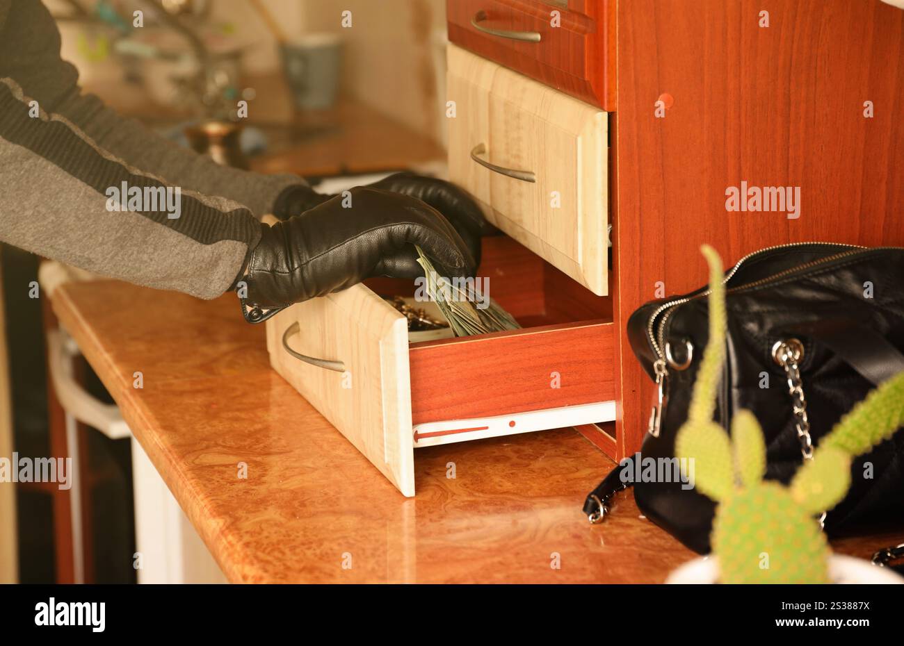 Robber in black outfit and gloves see in opened shelf in kitchen. The ...