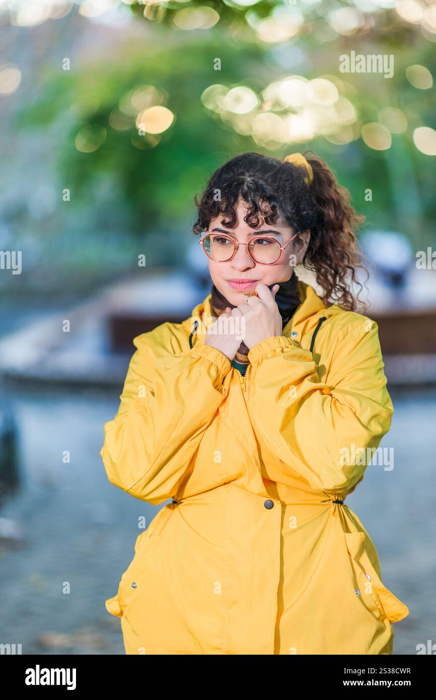 Young woman wearing yellow raincoat and eyeglasses feeling cold in a ...