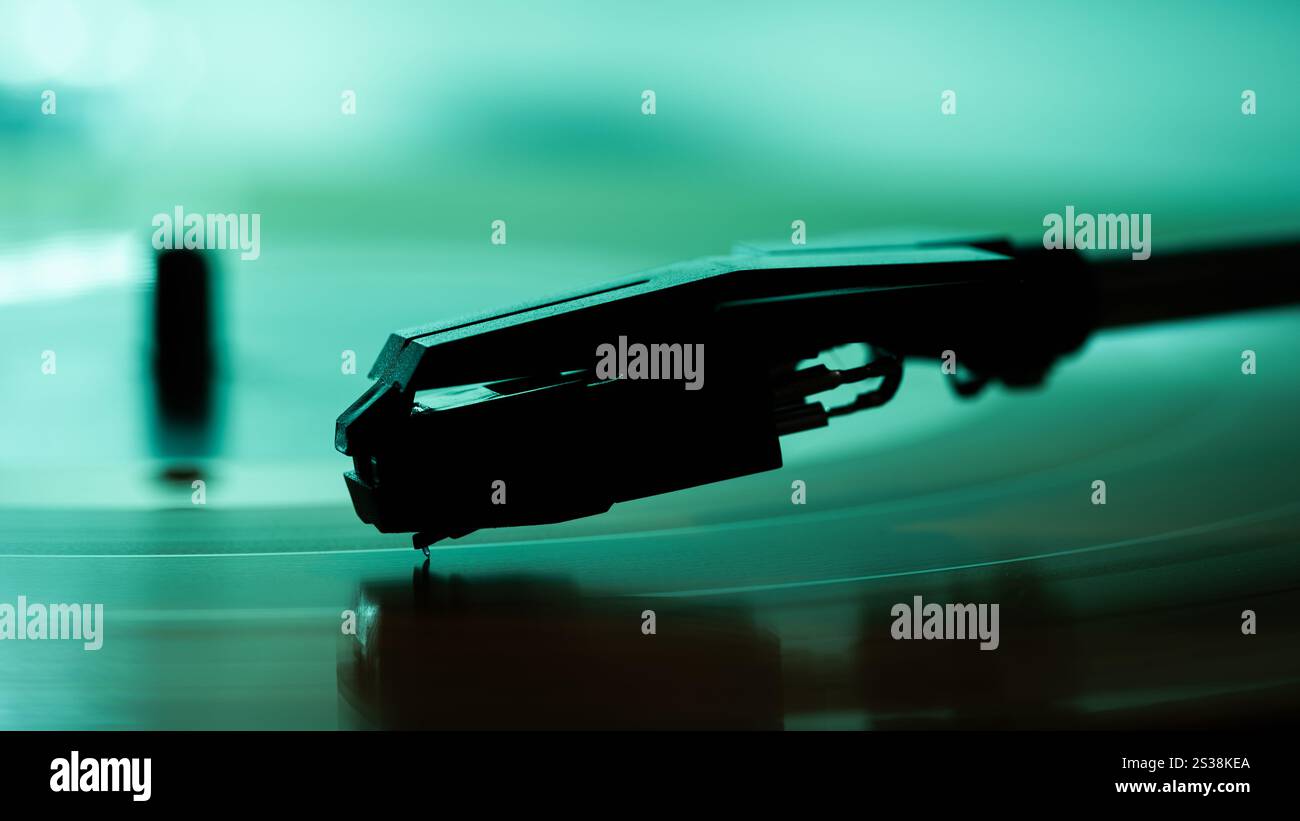 A close-up record player needle on a vinyl record with a teal ...