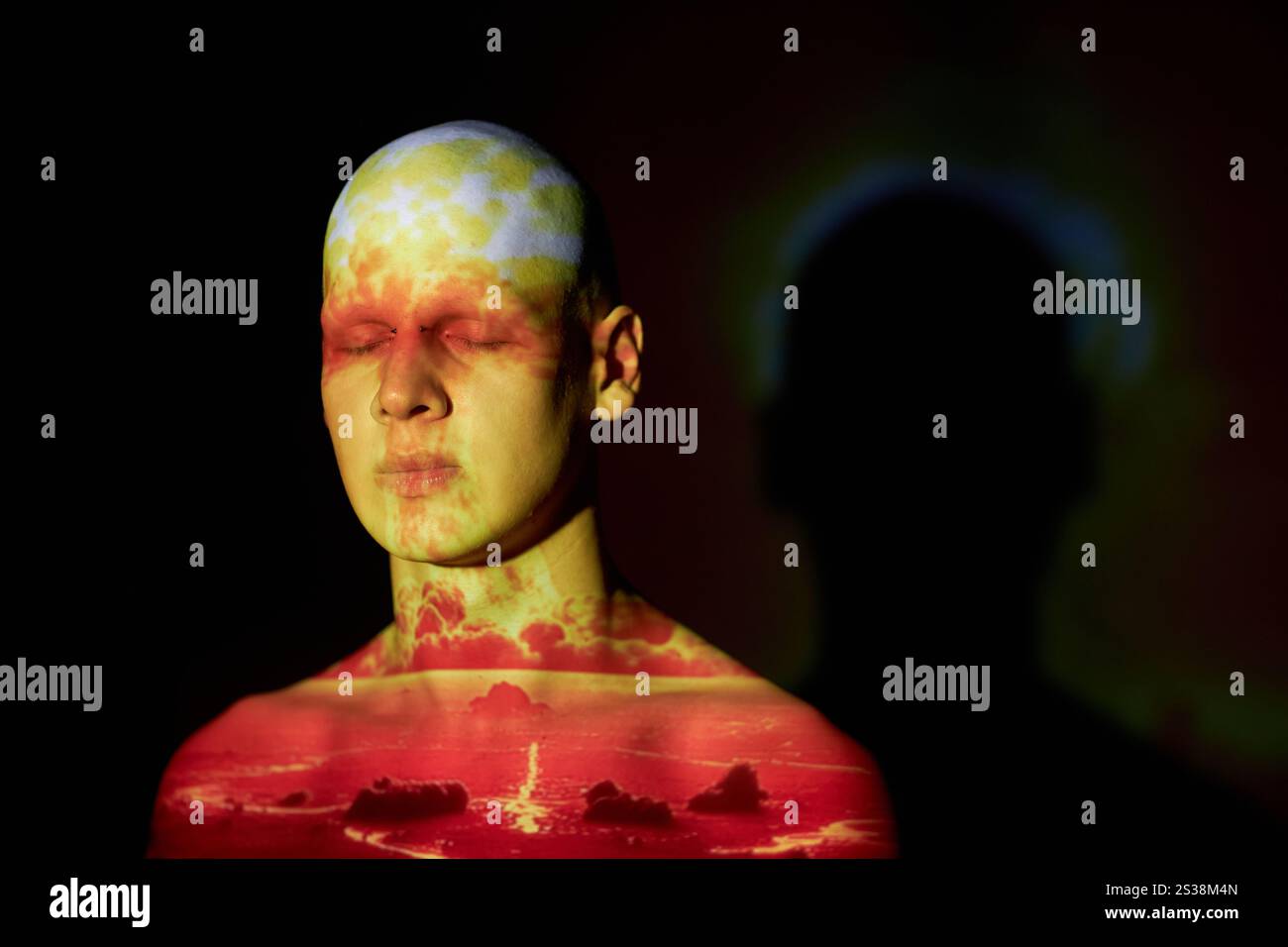 Portrait of emotionless bald man with eyes closed standing in light of ...