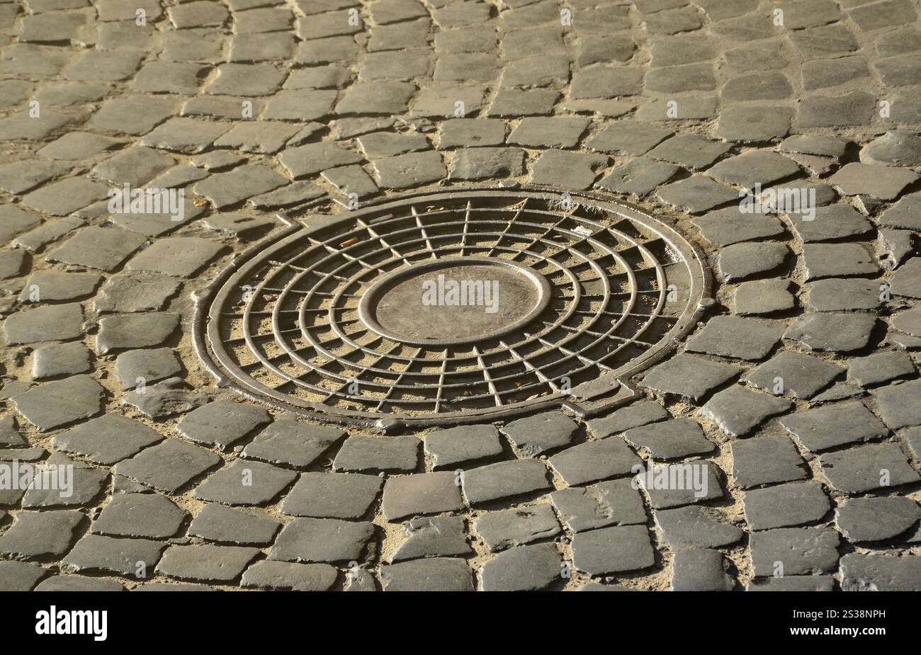 Old metal sewer hatch in the middle of the road, laid out of a smooth ...