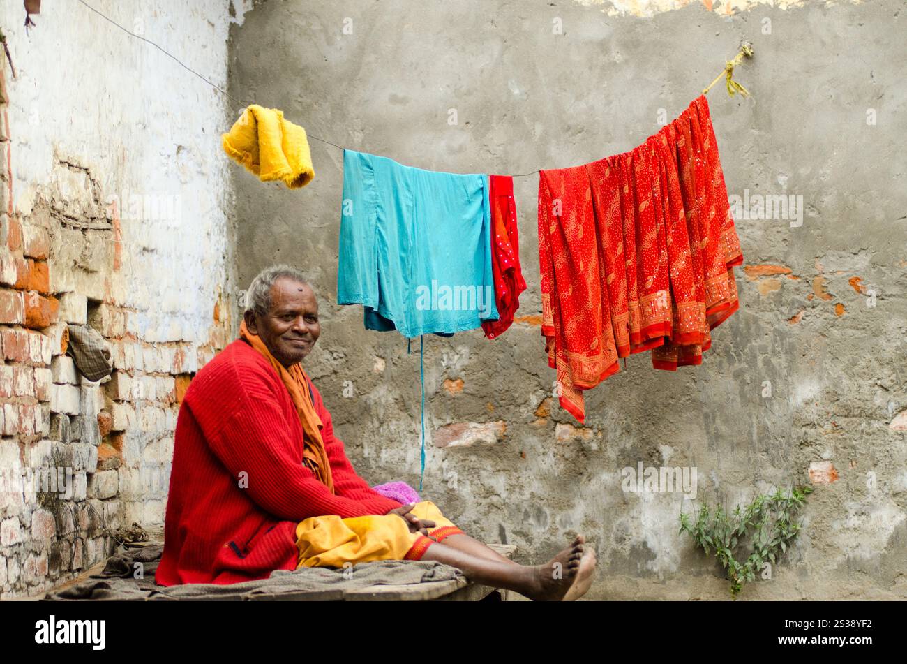 Man in traditional attire sitting outdoors against a weathered wall in ...
