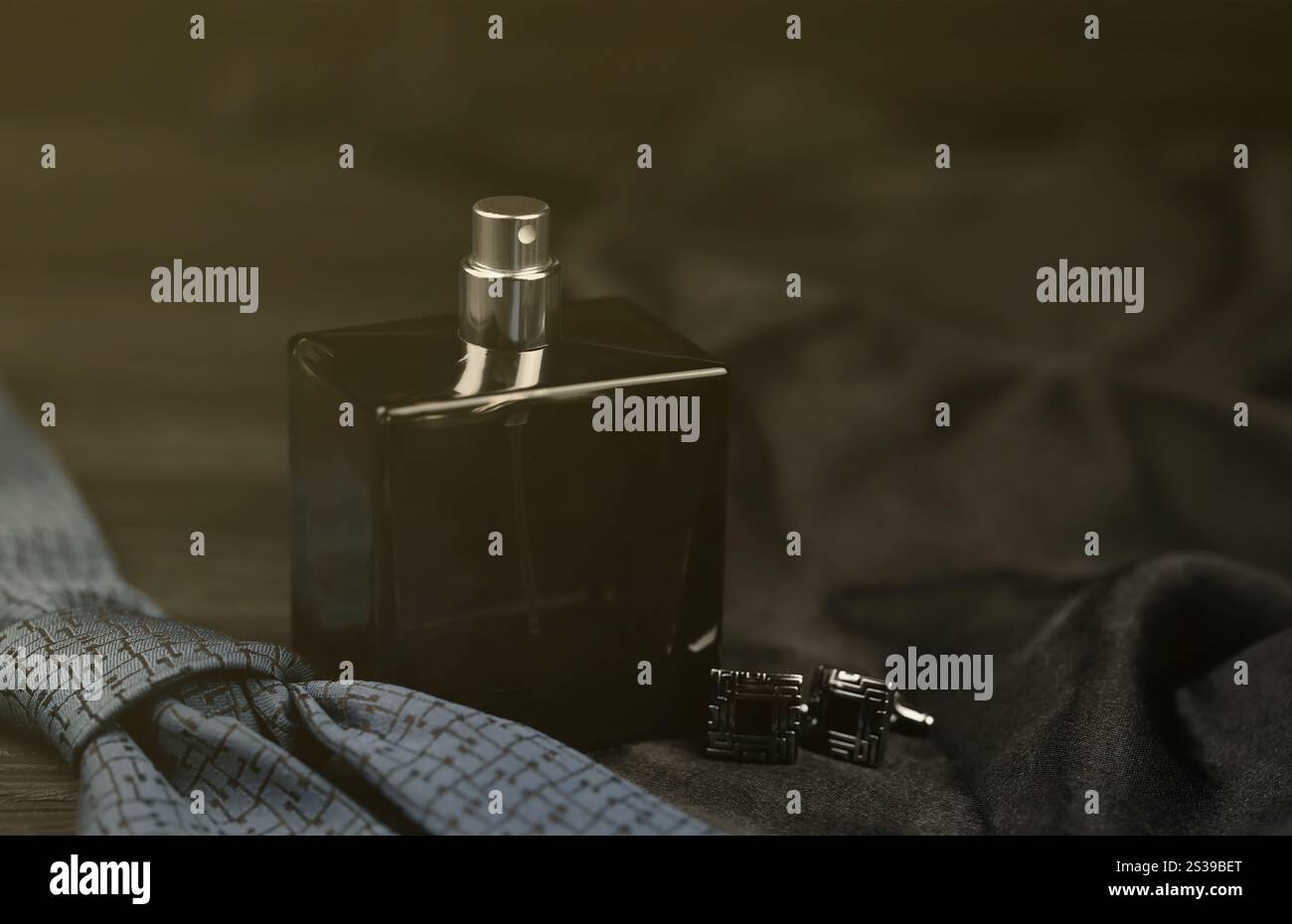 A bottle of mens cologne and cufflinks with blue tie lie on a black ...