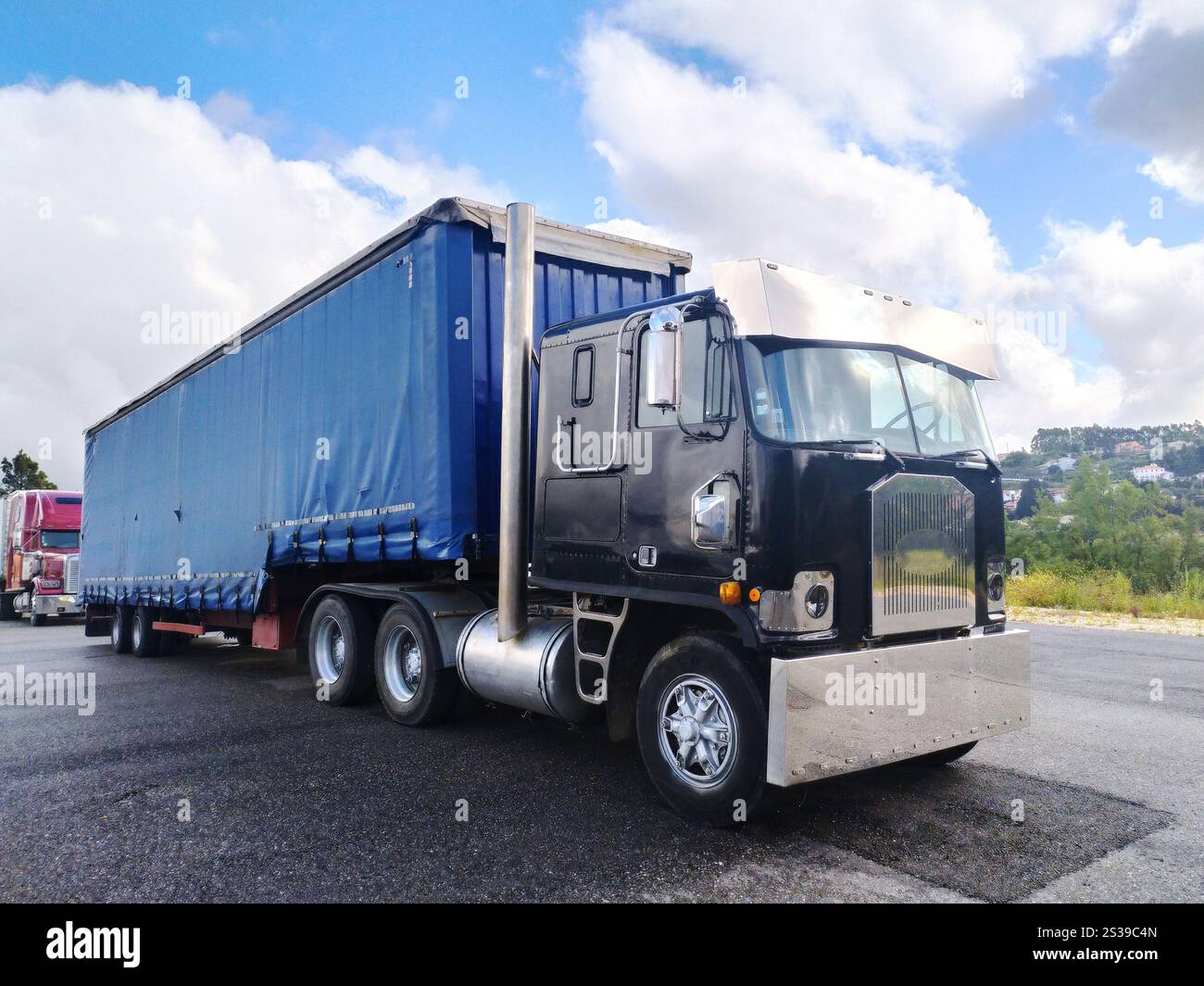A black retro semi truck is parked on the side of the road, with no one ...