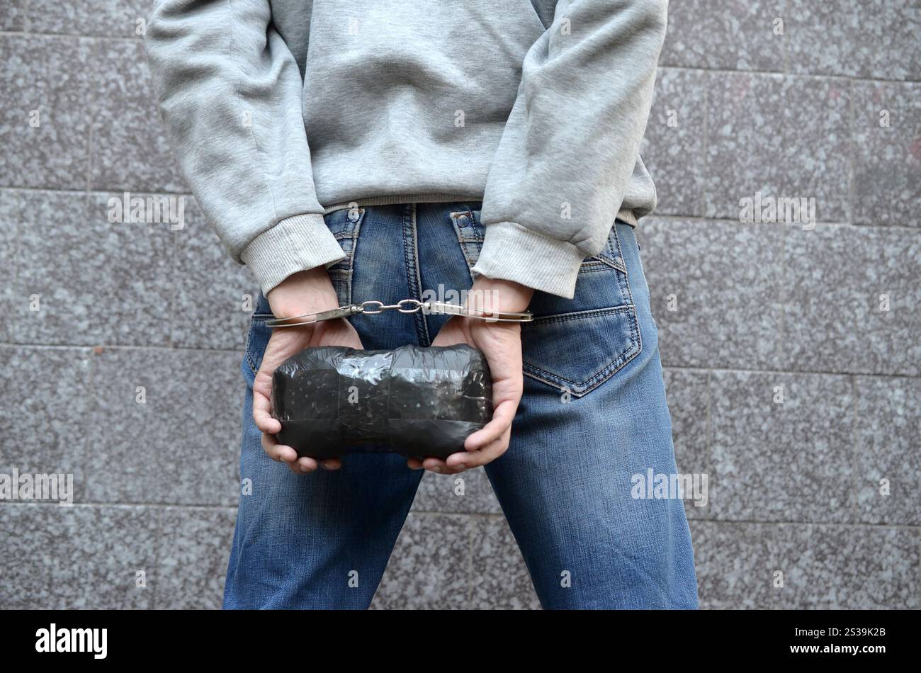 Arrested drug dealer in handcuffs with big heroin drug package on dark ...