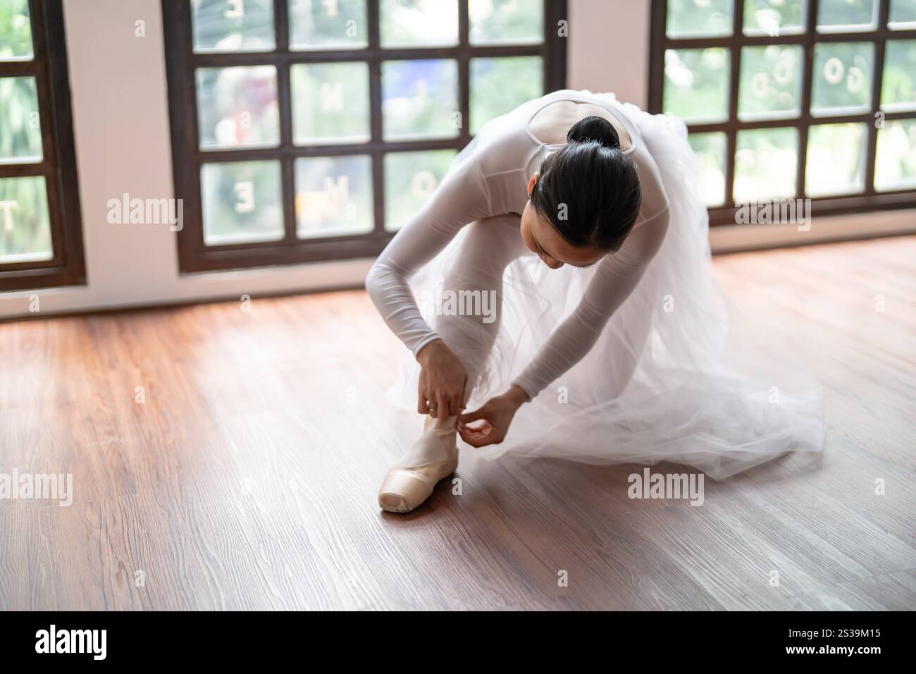 Ballerina in ballet shoes. Asian girl tying ribbons of toe shoes ...