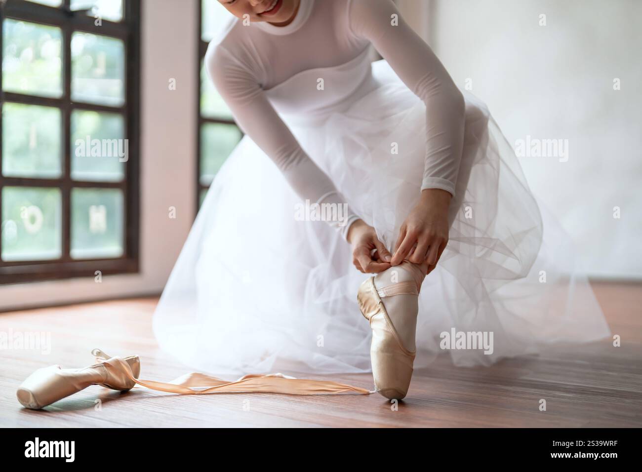 Ballerina in ballet shoes. Asian girl tying ribbons of toe shoes ...