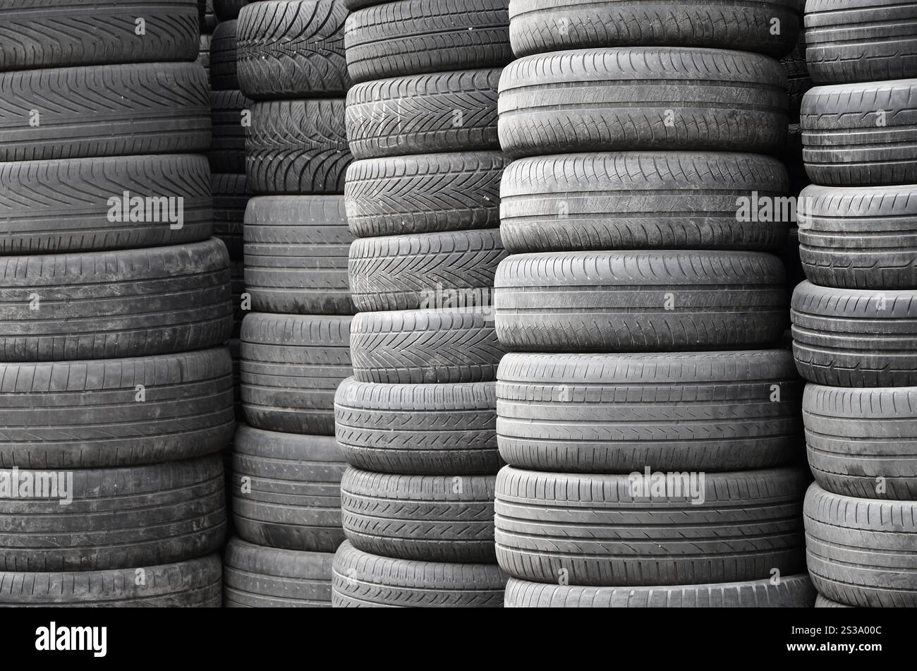 Old used tires stacked with high piles in secondary car parts shop garage close up. Old used ...