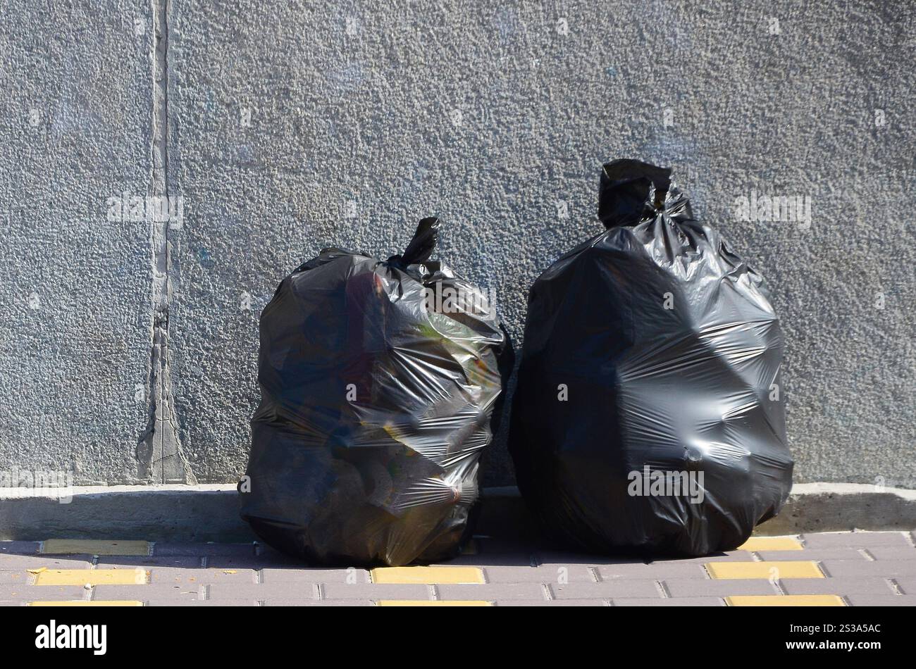Two black garbage bags on tiled street floor at concrete fence in city ...