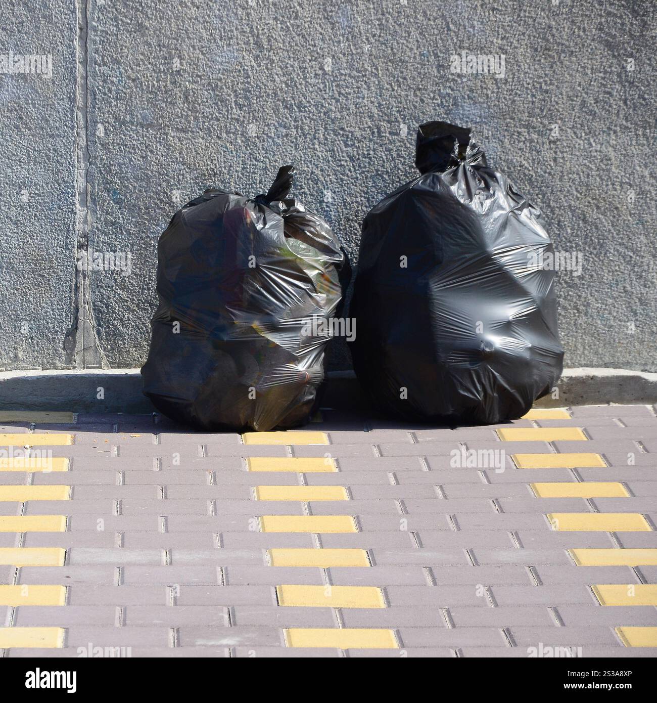 Two black garbage bags on tiled street floor at concrete fence in city ...