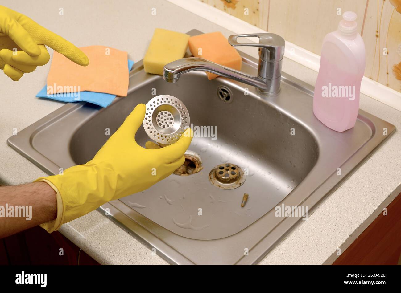 Cleaner in rubber gloves shows clean plughole protector of a kitchen ...