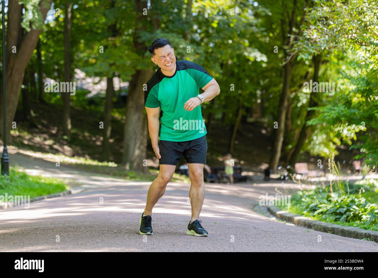 Asian runner athlete with knee pain in park. Japanese man massaging ...