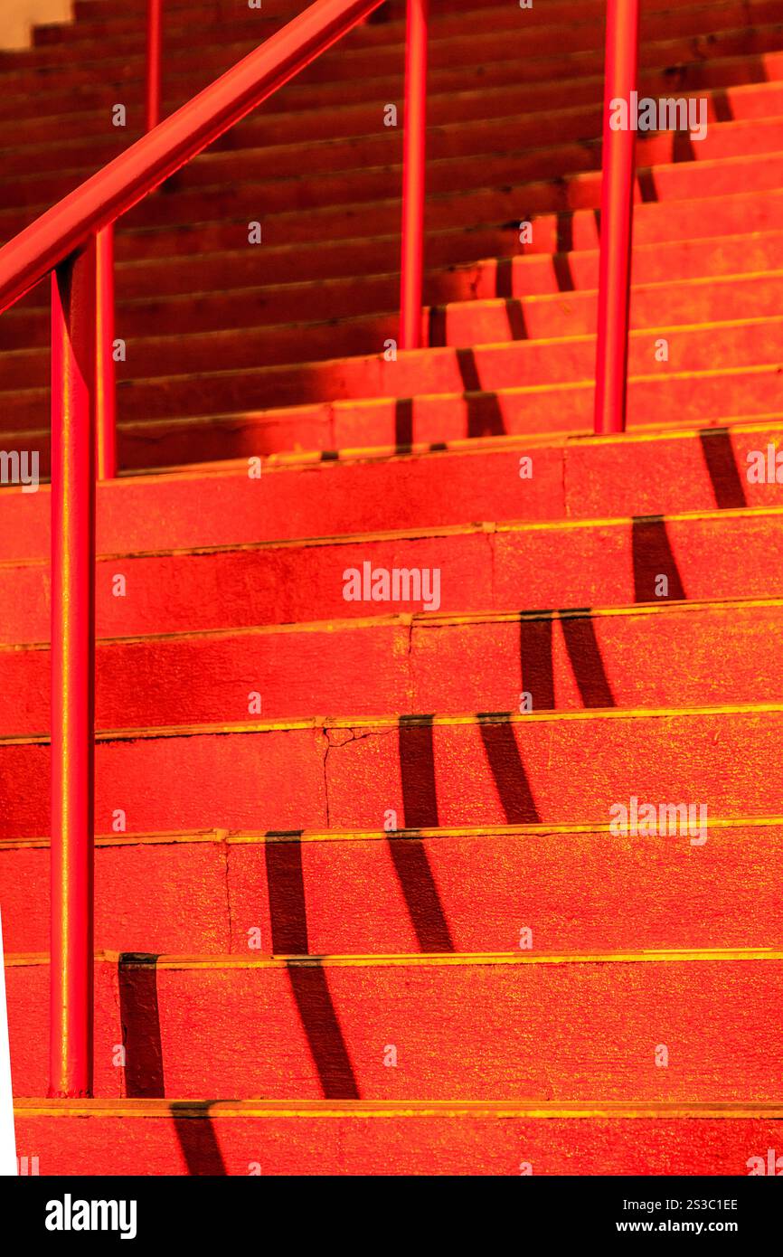 A staircase with red steps and a red railing. The stairs are shadowed ...