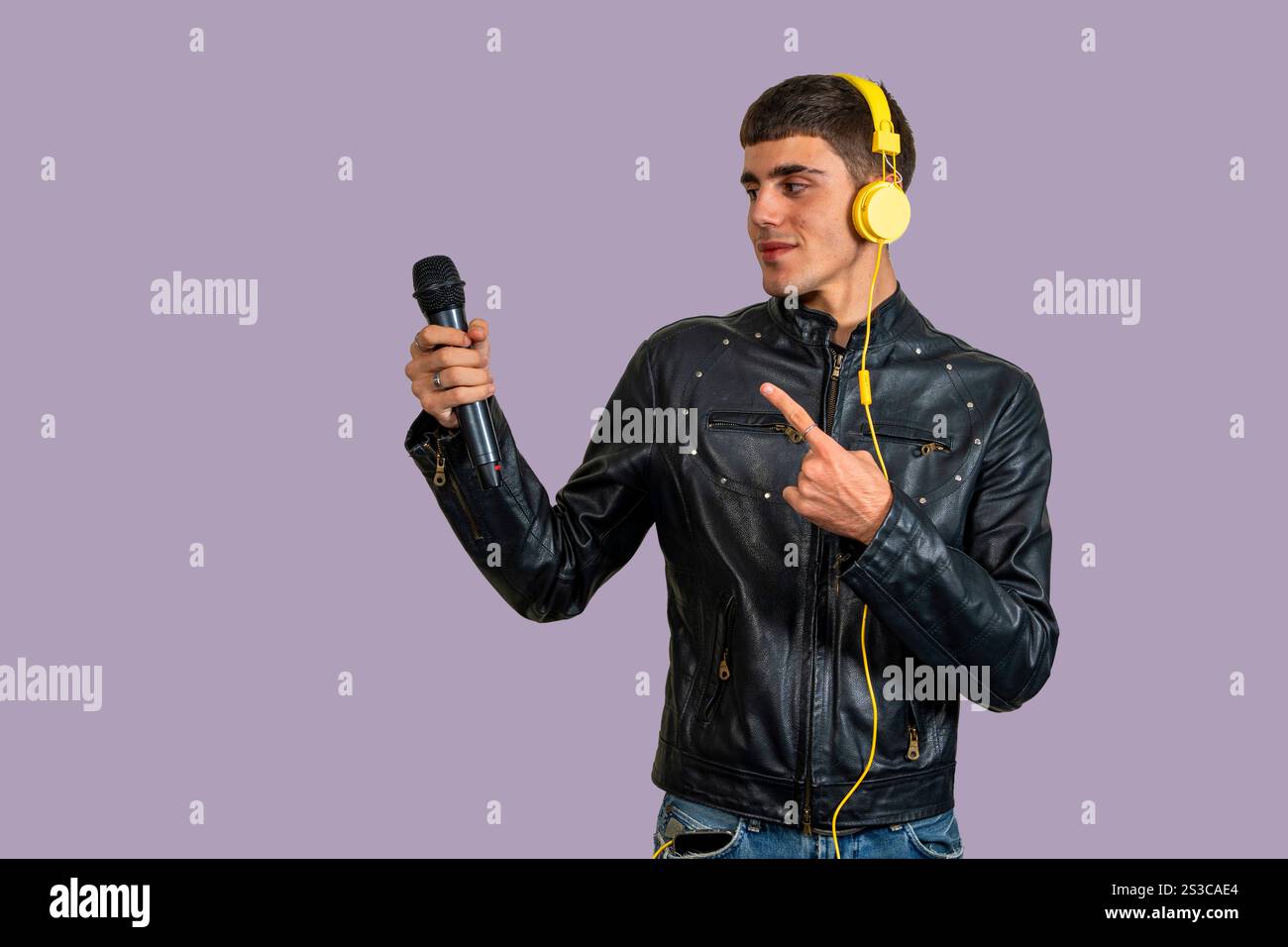 Stylish young man wearing headphones pointing at a wireless microphone while singing Stock Photo ...