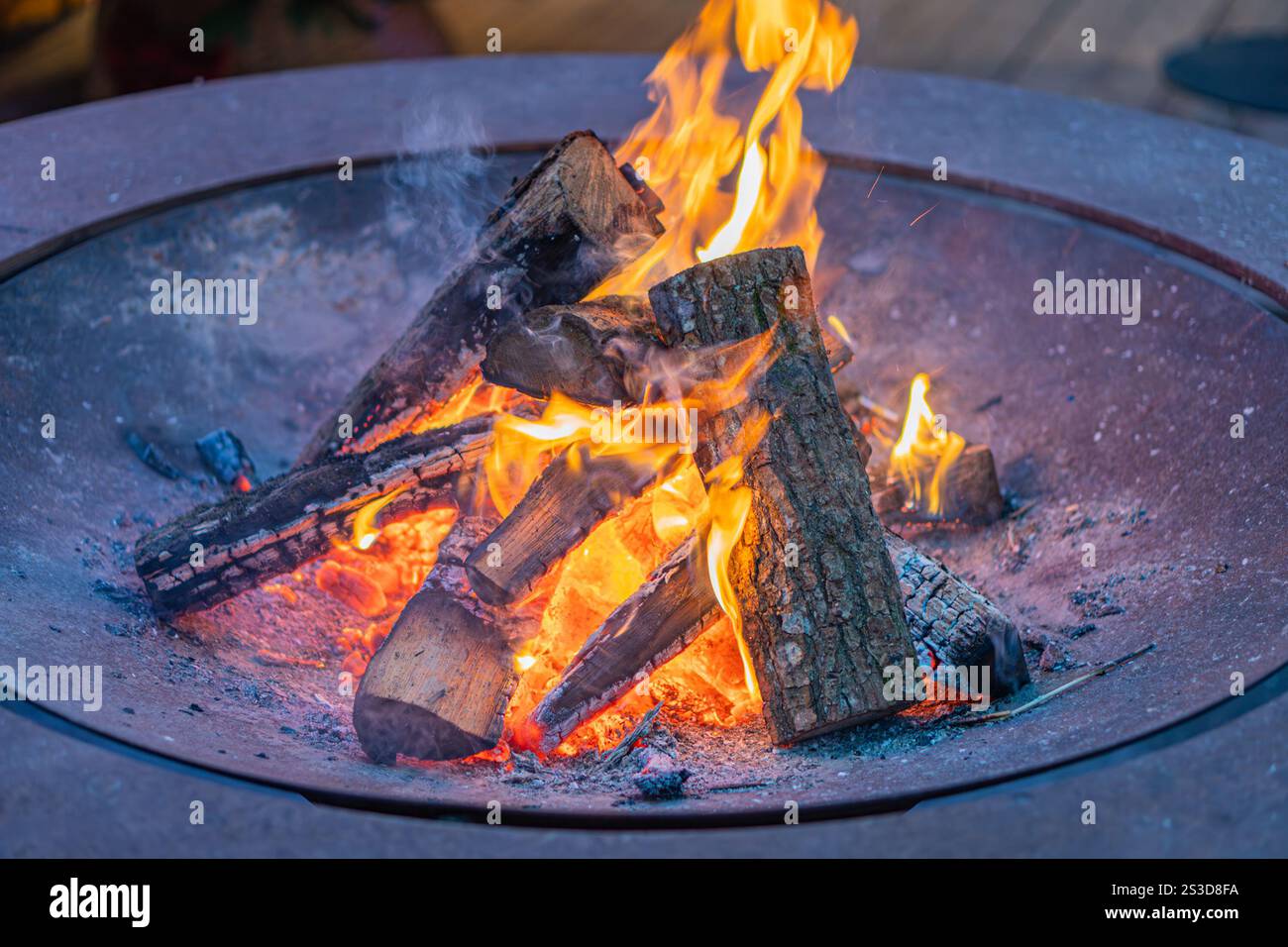 Image depicts a nighttime fire pit, surrounded by burning logs within a ...