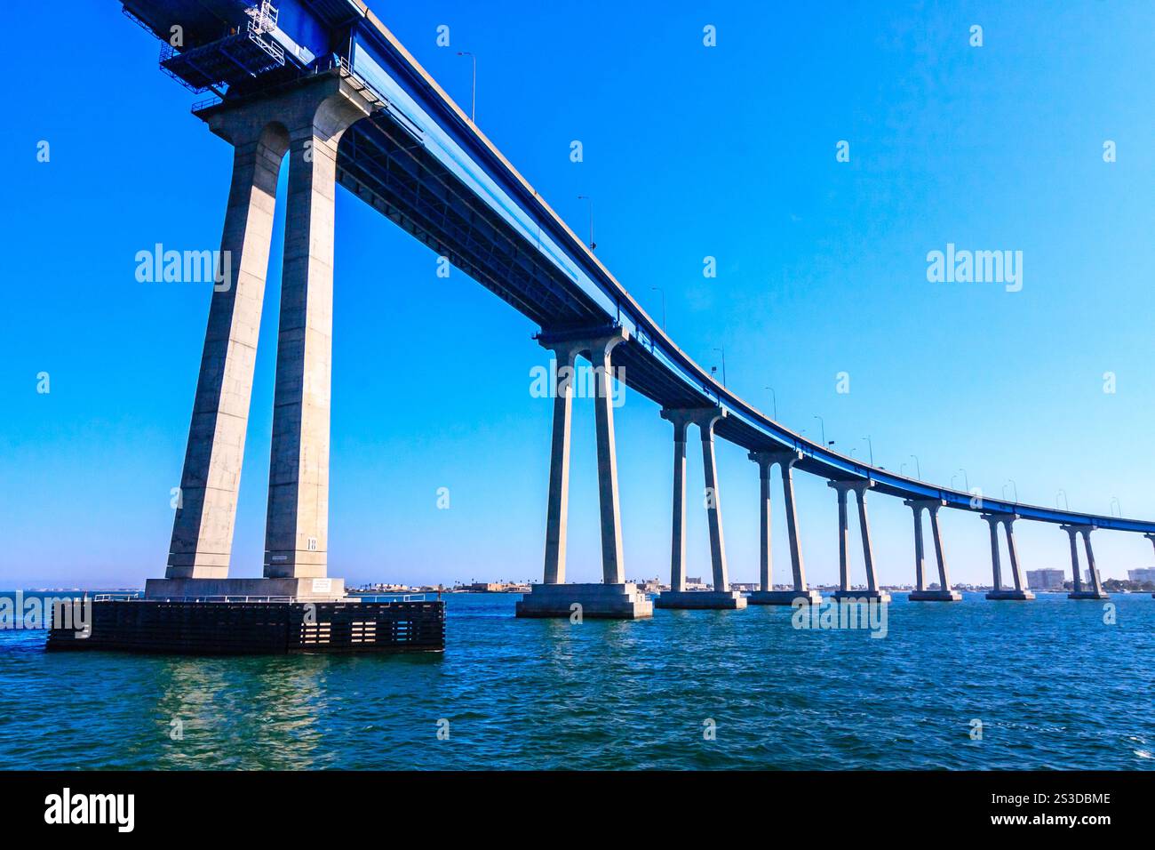 A long bridge spans a body of water. The bridge is blue and the sky is ...