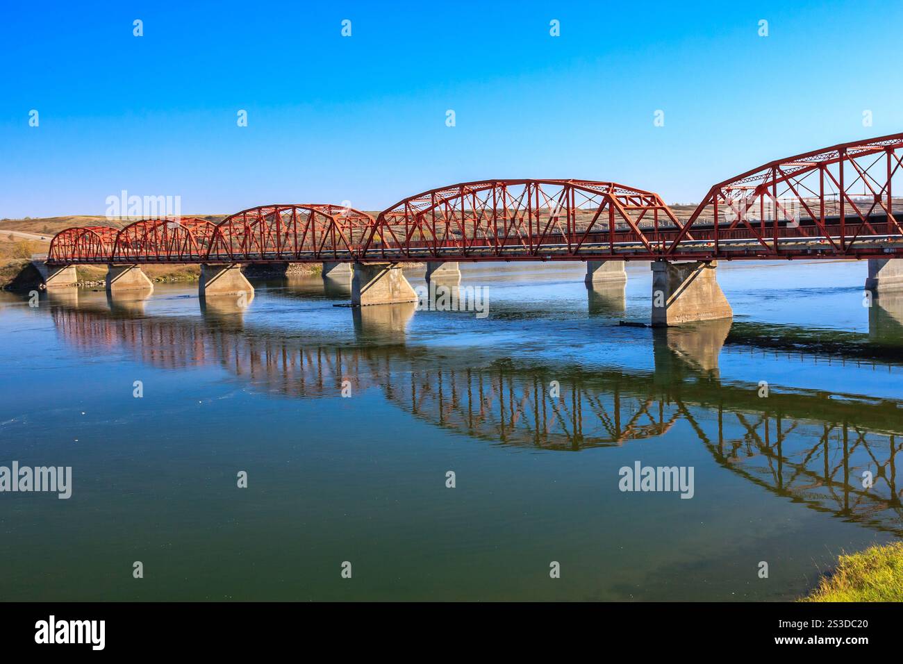 A red bridge spans a river, with the water reflecting the bridge's red ...