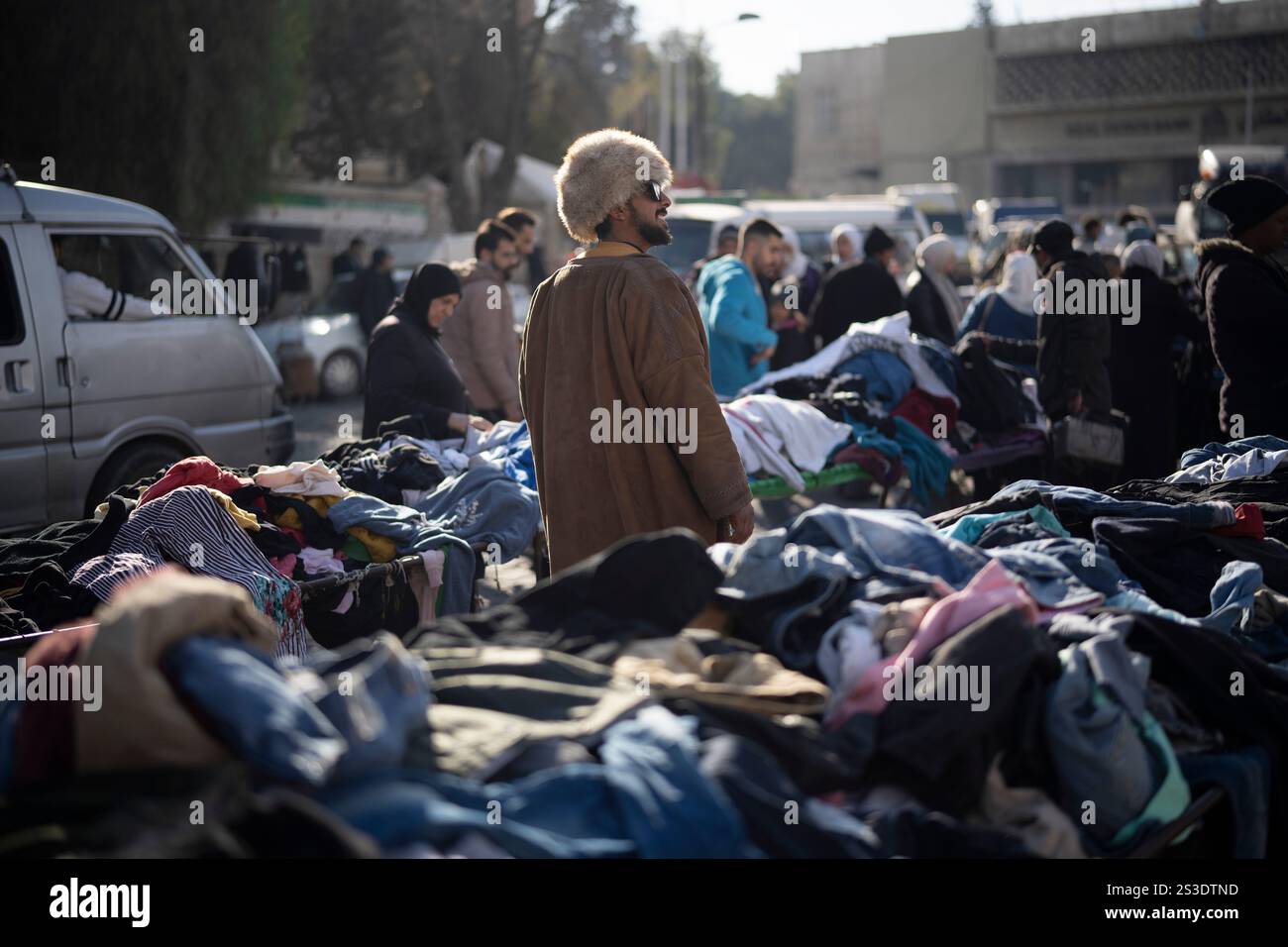 A street vendor walks amidst his stalls displaying second hand clothes ...