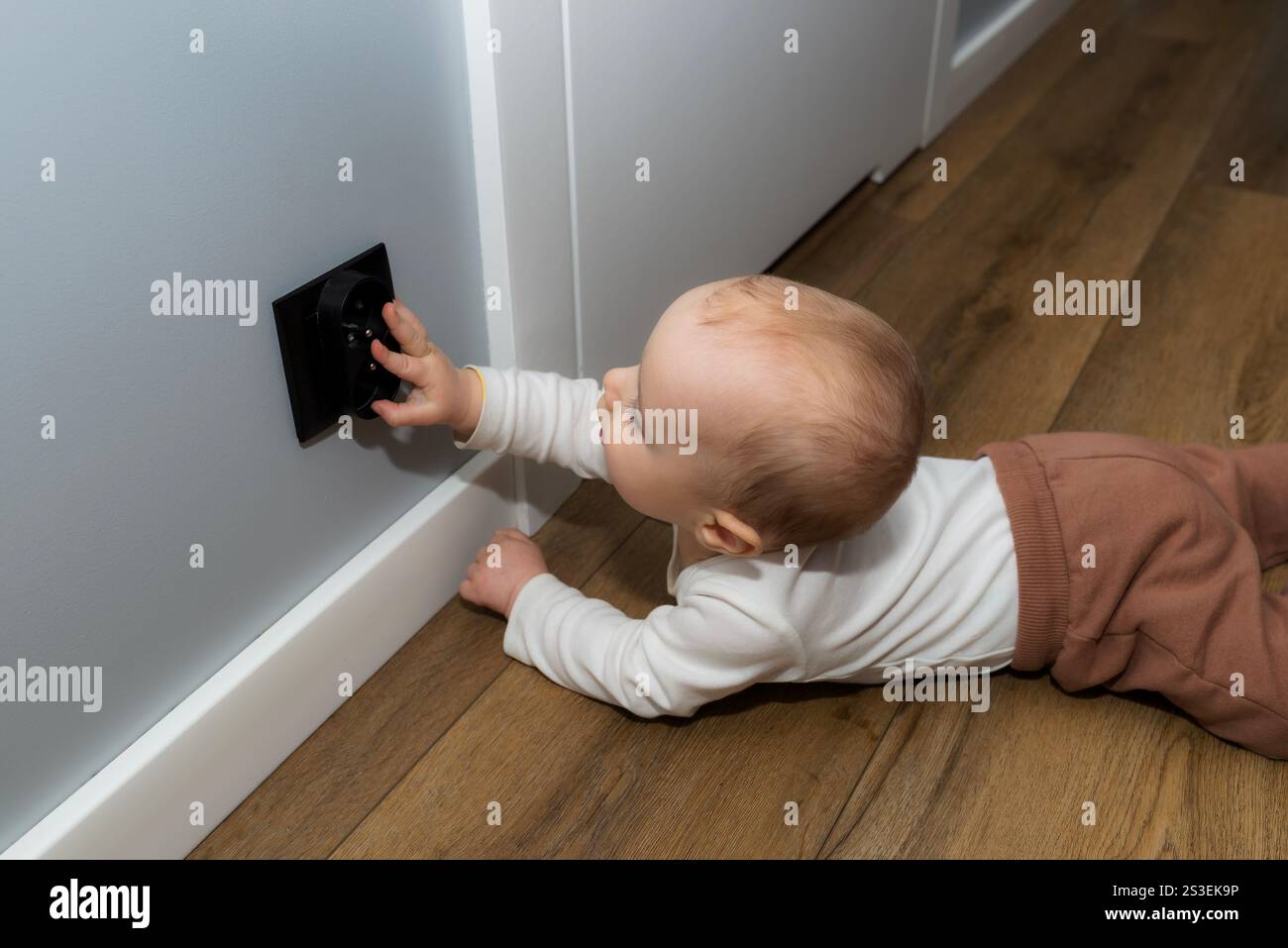 A seven-month-old Caucasian baby touches a black electrical outlet on ...