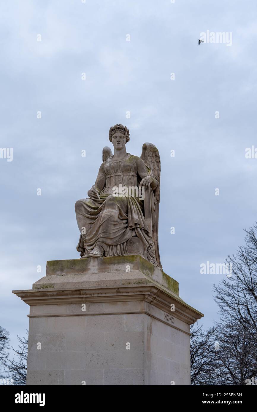 Statue of a winged figure seated on a pedestal under an overcast sky ...