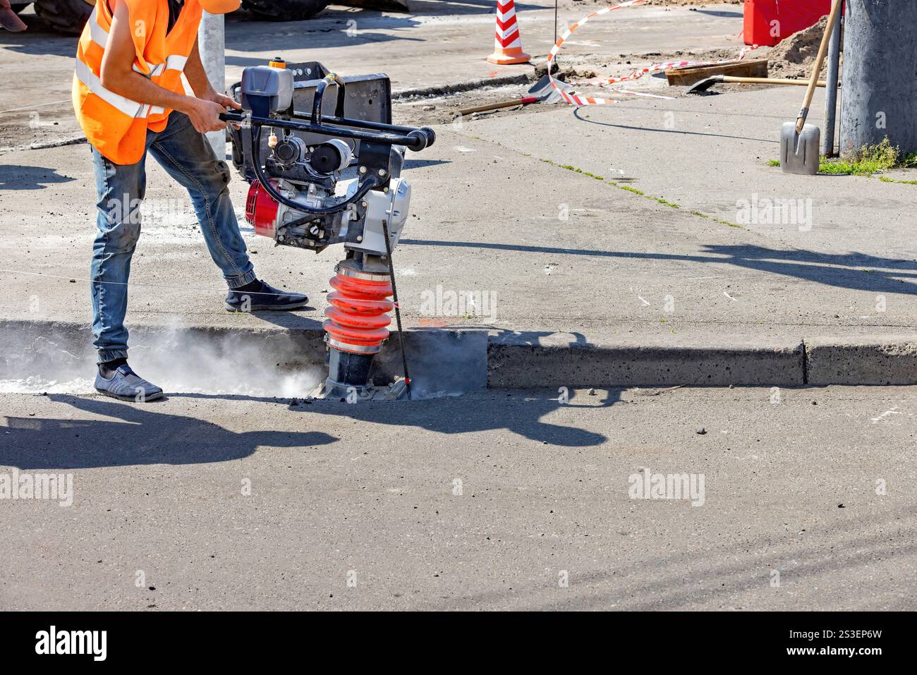 Construction worker using equipment to break concrete on a sunny day ...