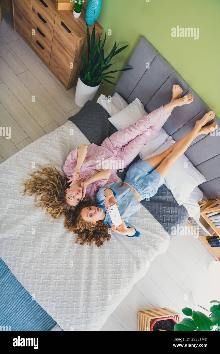 Vertical full length photo of two young females lying bed upside down ...