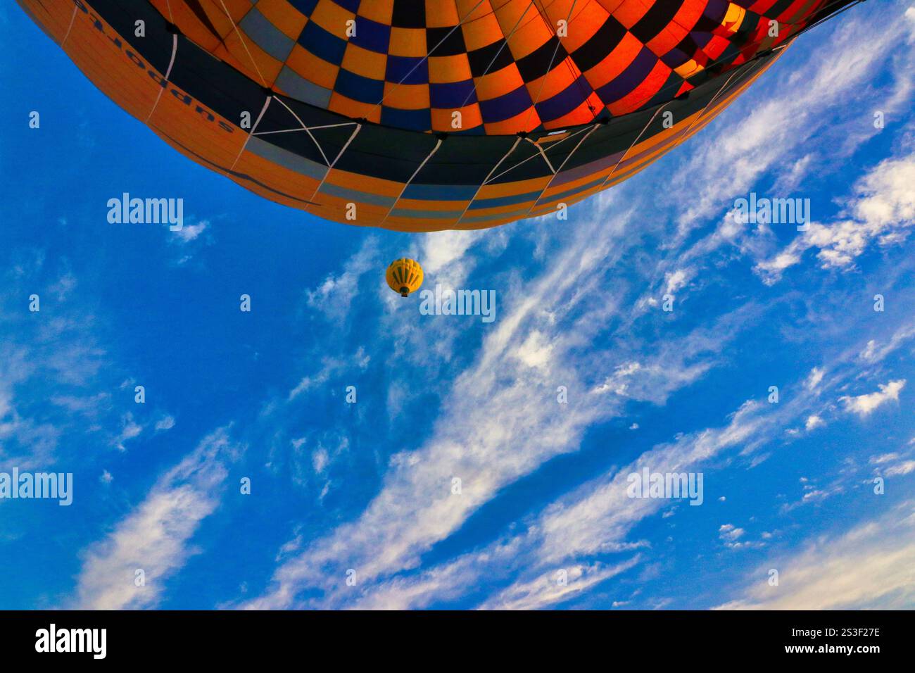 A hot air balloon rises into cloud streaked blue skies taking tourists ...
