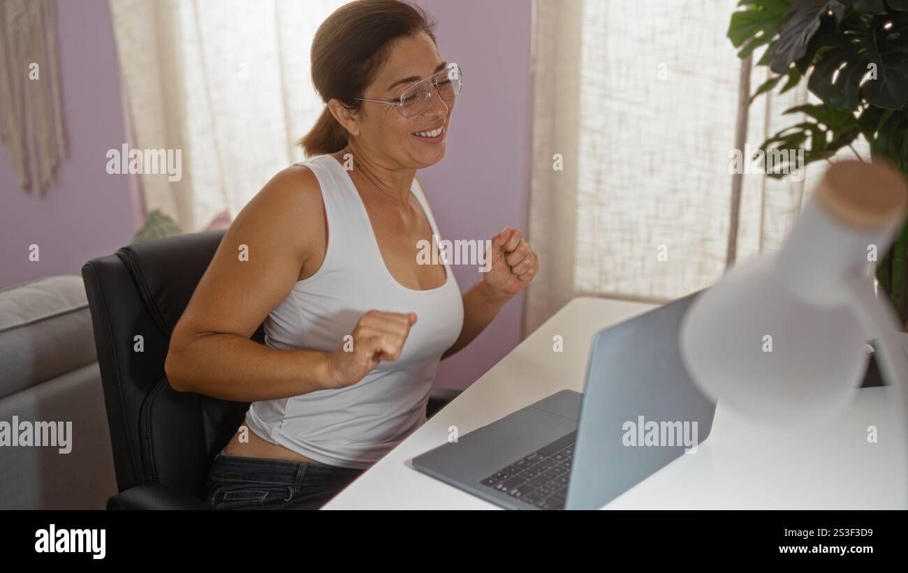 Woman dancing happily while working on a laptop in a cozy living room ...