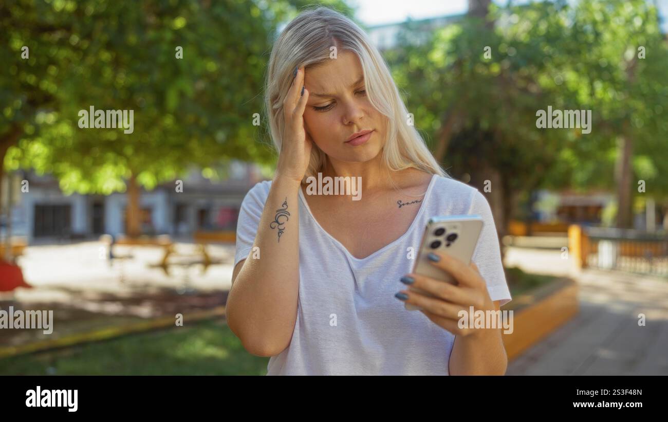 Blonde woman checking smartphone in urban park with a concerned look ...