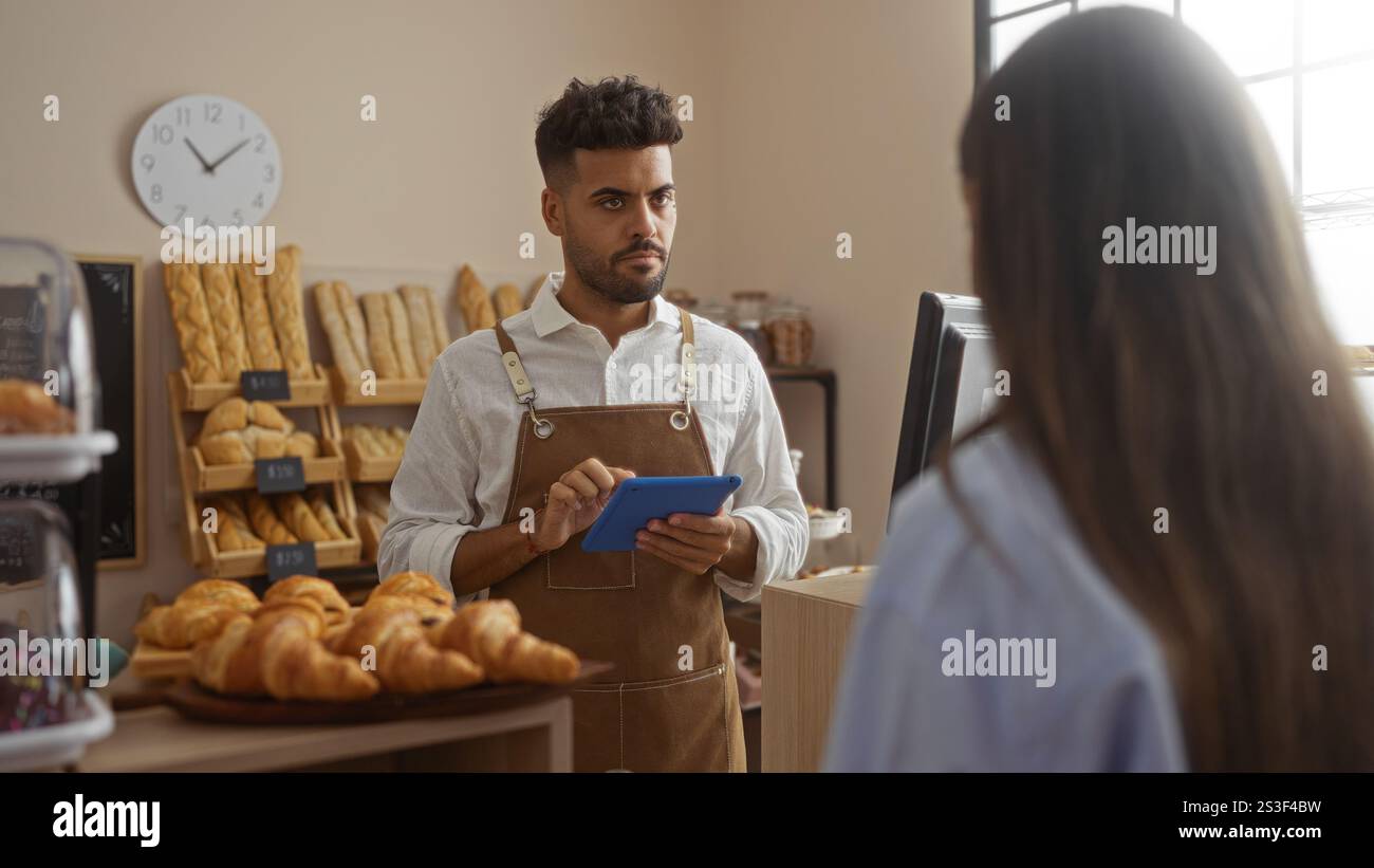 Man in brown apron using tablet with woman customer in bakery shop ...