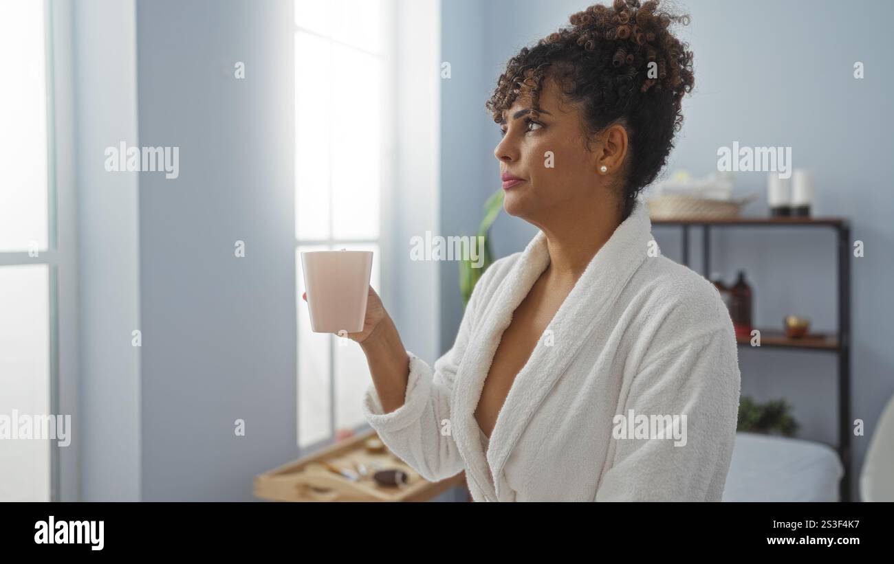 Young woman relaxing in a spa drinking a beverage wearing a white robe ...