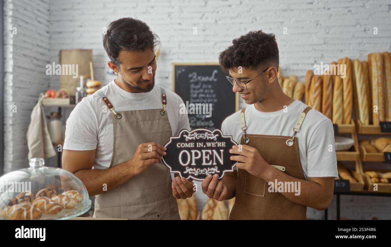Two hispanic male bakers holding an open sign together in an indoor ...