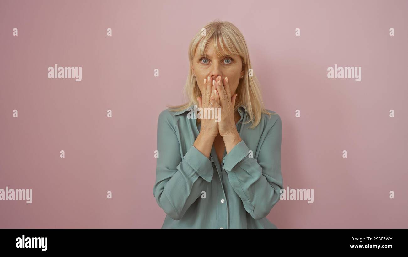 Woman covering her mouth in shock while standing against a pink ...