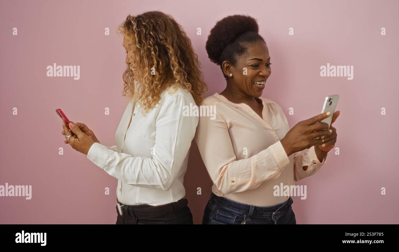 Women friends using phones together, standing against an isolated pink ...