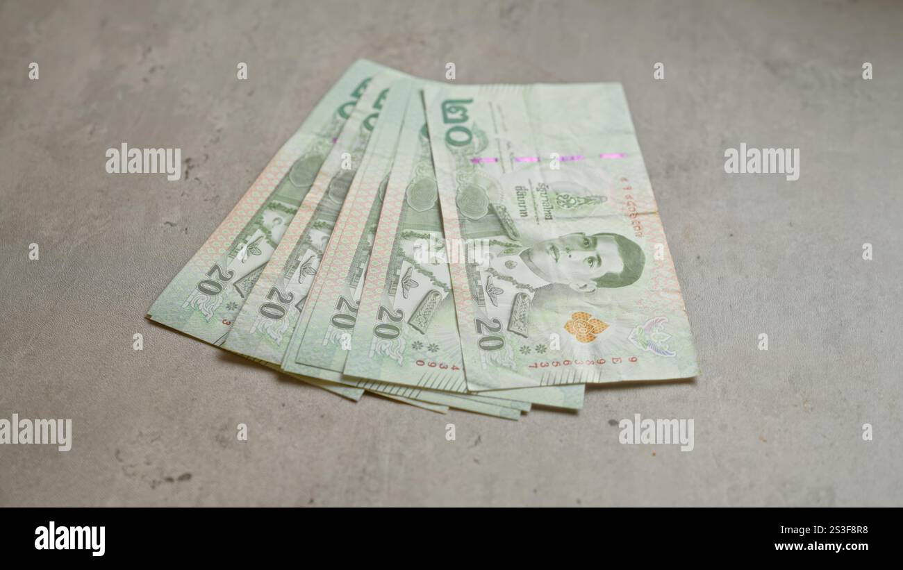 Stack of thai baht banknotes spread out on a concrete surface ...