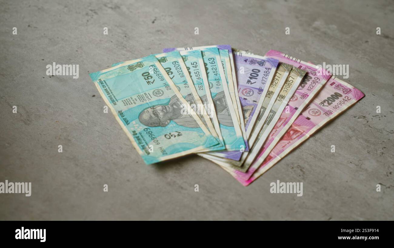 Indian banknotes of various denominations spread on a concrete surface ...