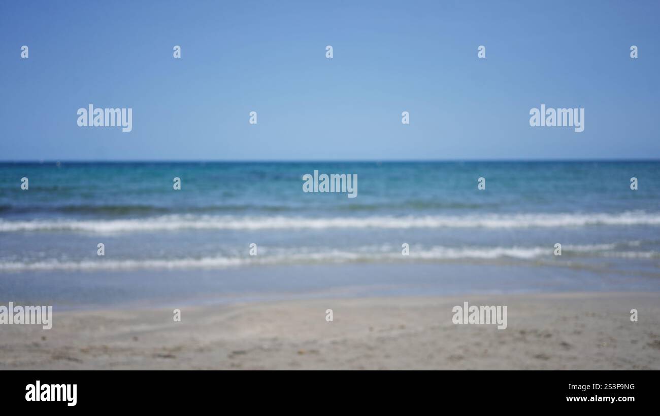Blurred view of an outdoor beach with defocused sand and sea waves ...
