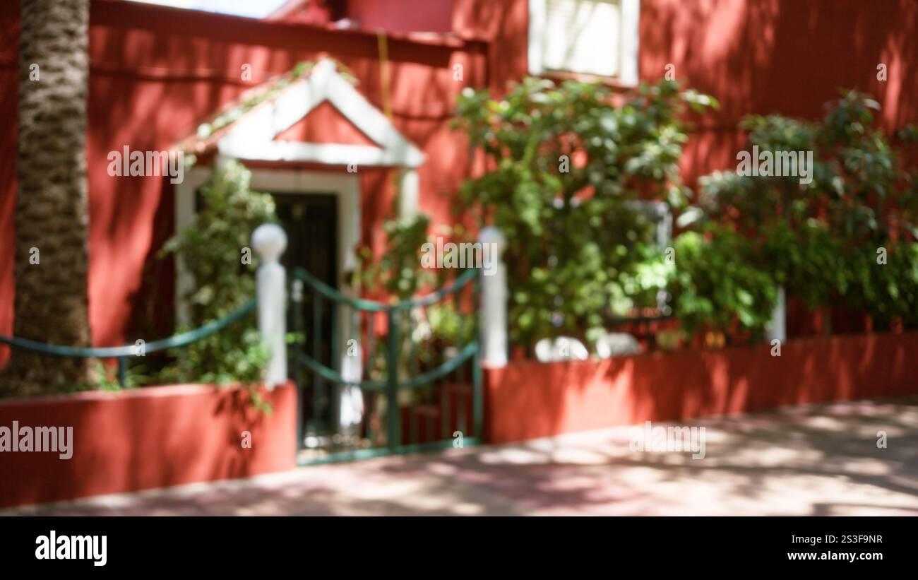 Defocused background image of a red house exterior with plants and a ...