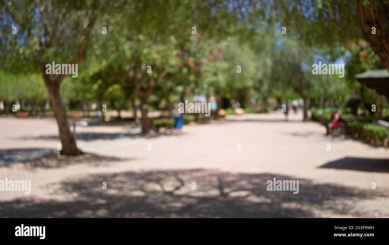 Outdoor blurred park scene with defocused trees, benches, people, and ...