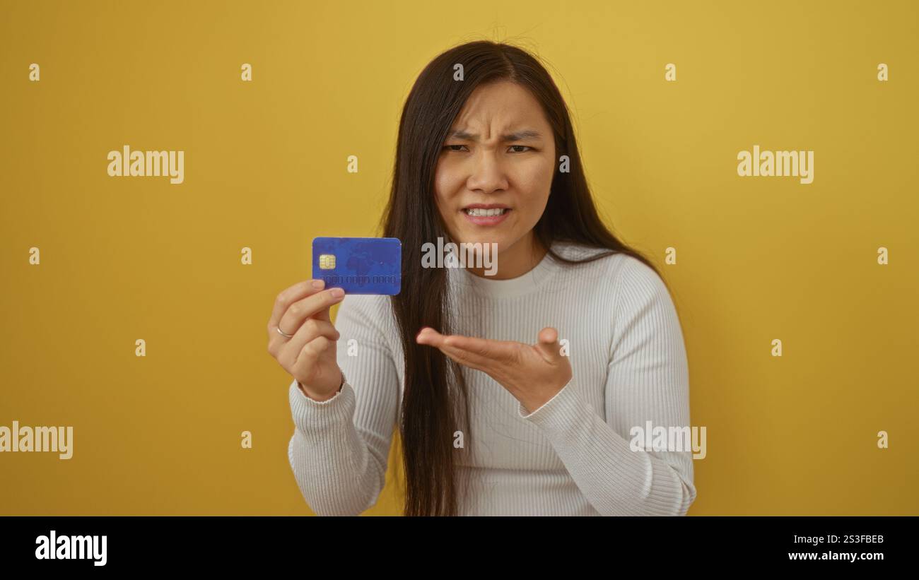 Woman holding credit card against yellow background looking puzzled and ...