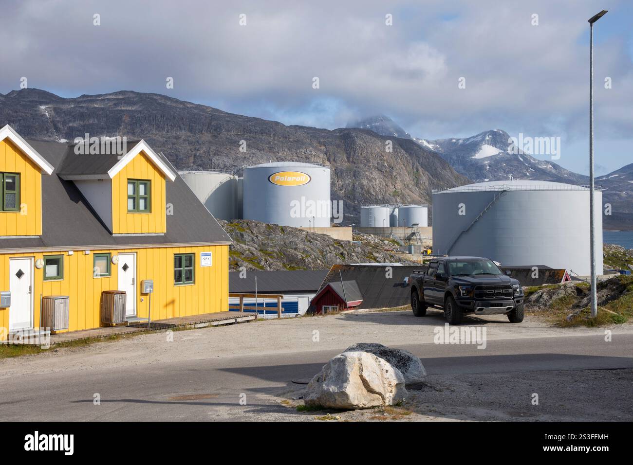Oil terminal with large fuel tanks and a yellow house against mountains ...