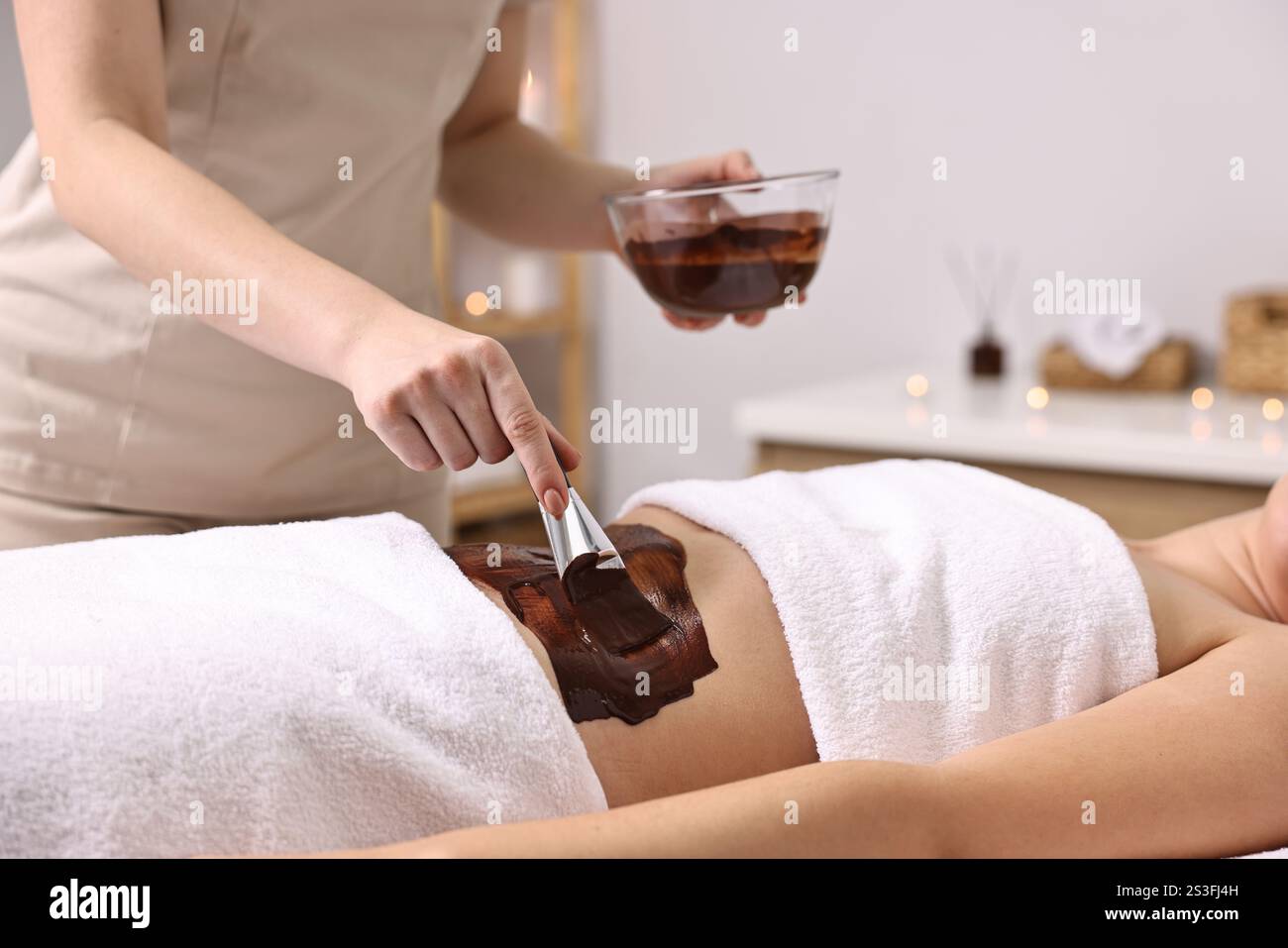 Chocolate body wrap. Spa worker applying mask onto woman's belly in ...