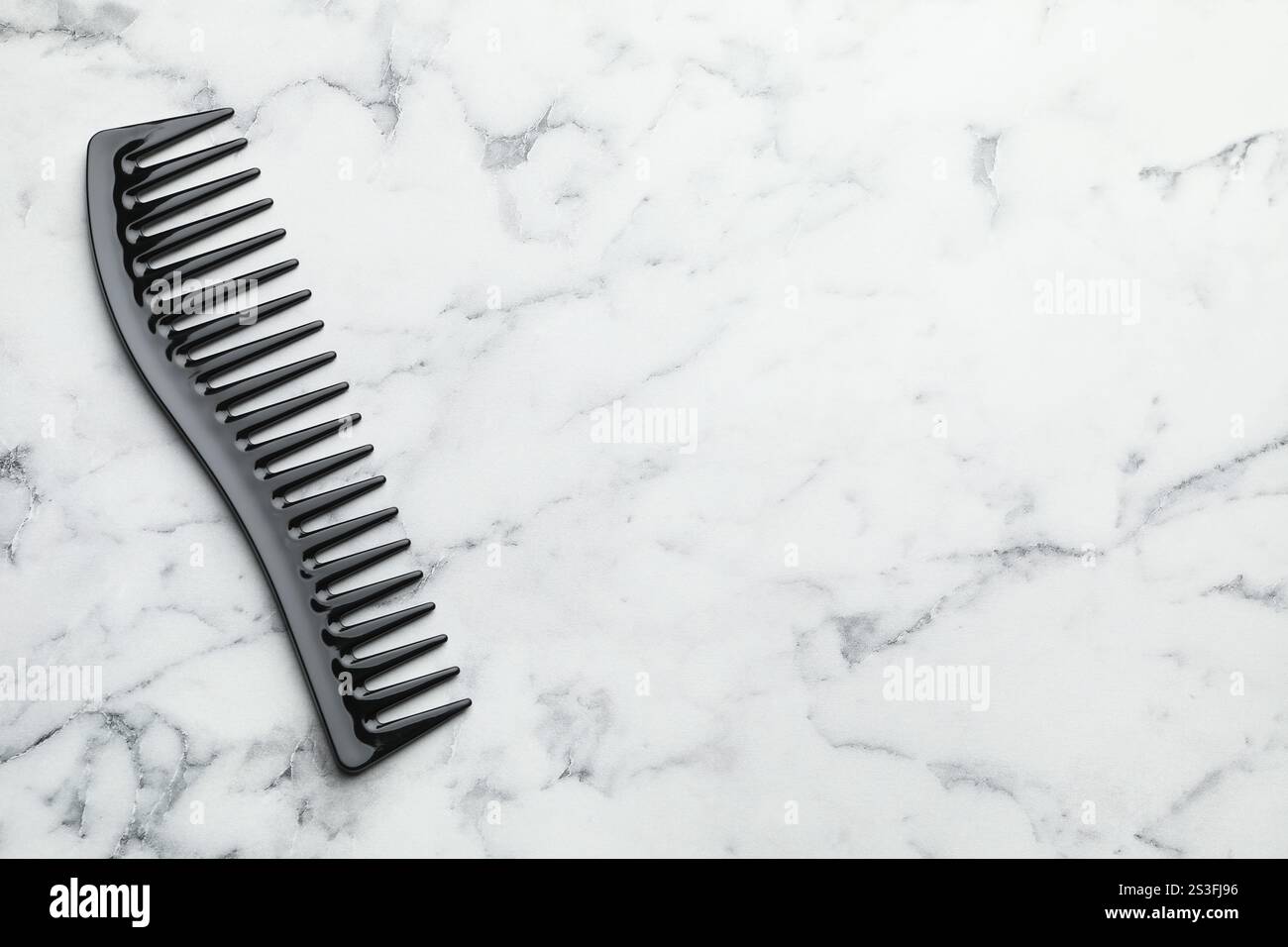 One black plastic comb on white marble table, top view. Space for text ...