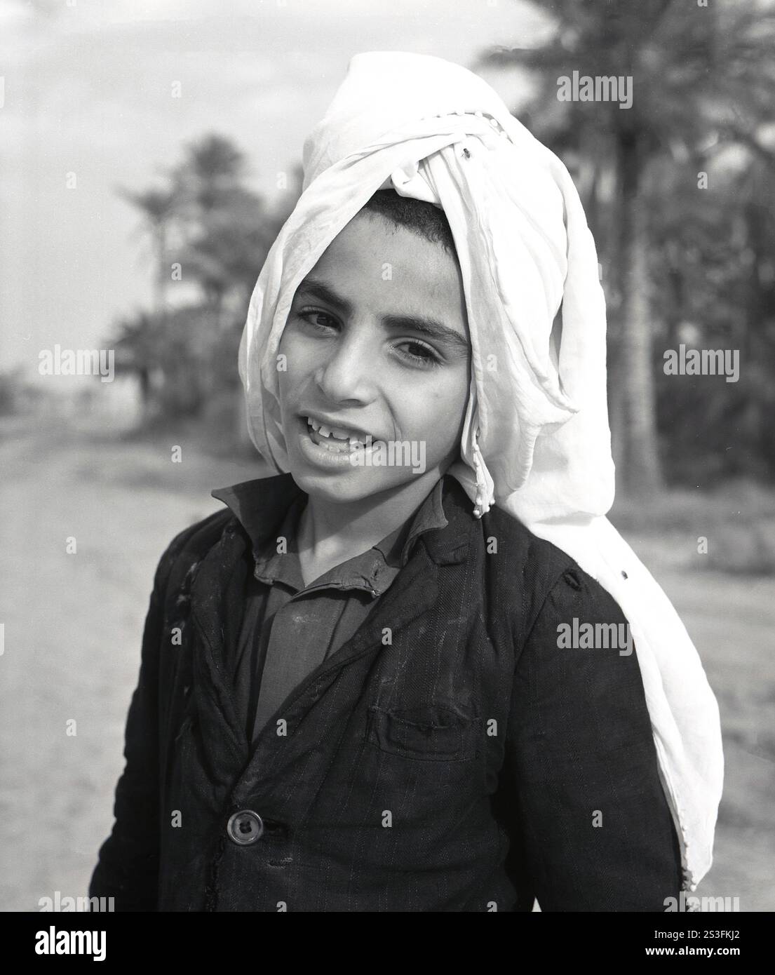 1950s, historical photo by J Allan Cash of a young arab boy outside, wearing a long cotton ...